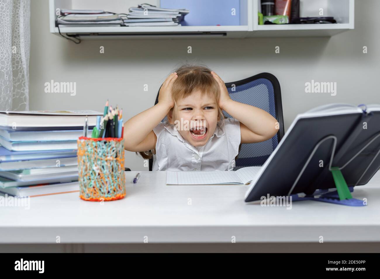 unhappy little girl bored with homework. baby screams clutching his ...