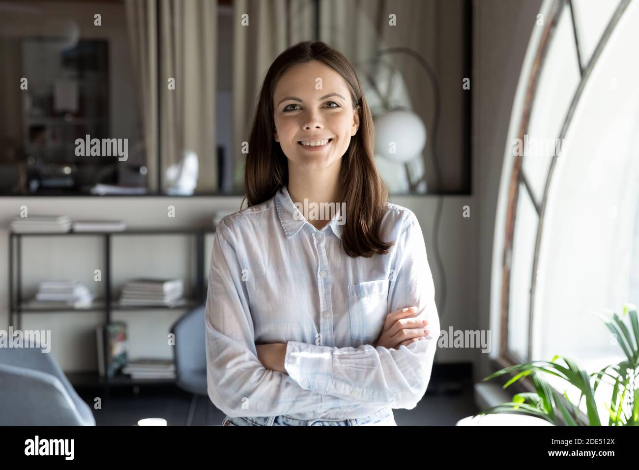 Motivated young lady employee standing at office looking at camera ...