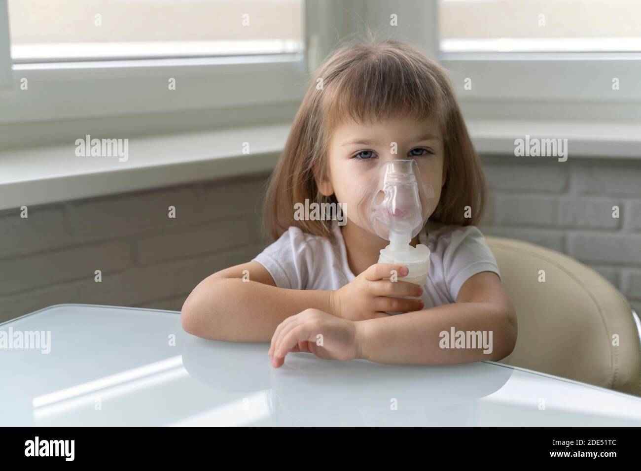 kid girl makes inhalation with a nebulizer at home, sitting on a chair ...
