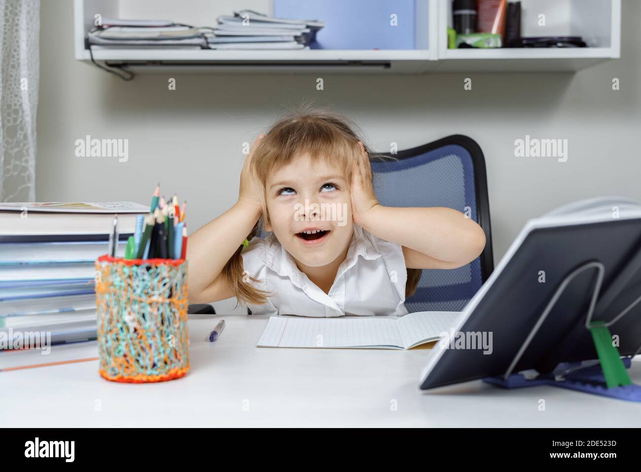 little girl doing homework at the table. hands on head, emotional ...