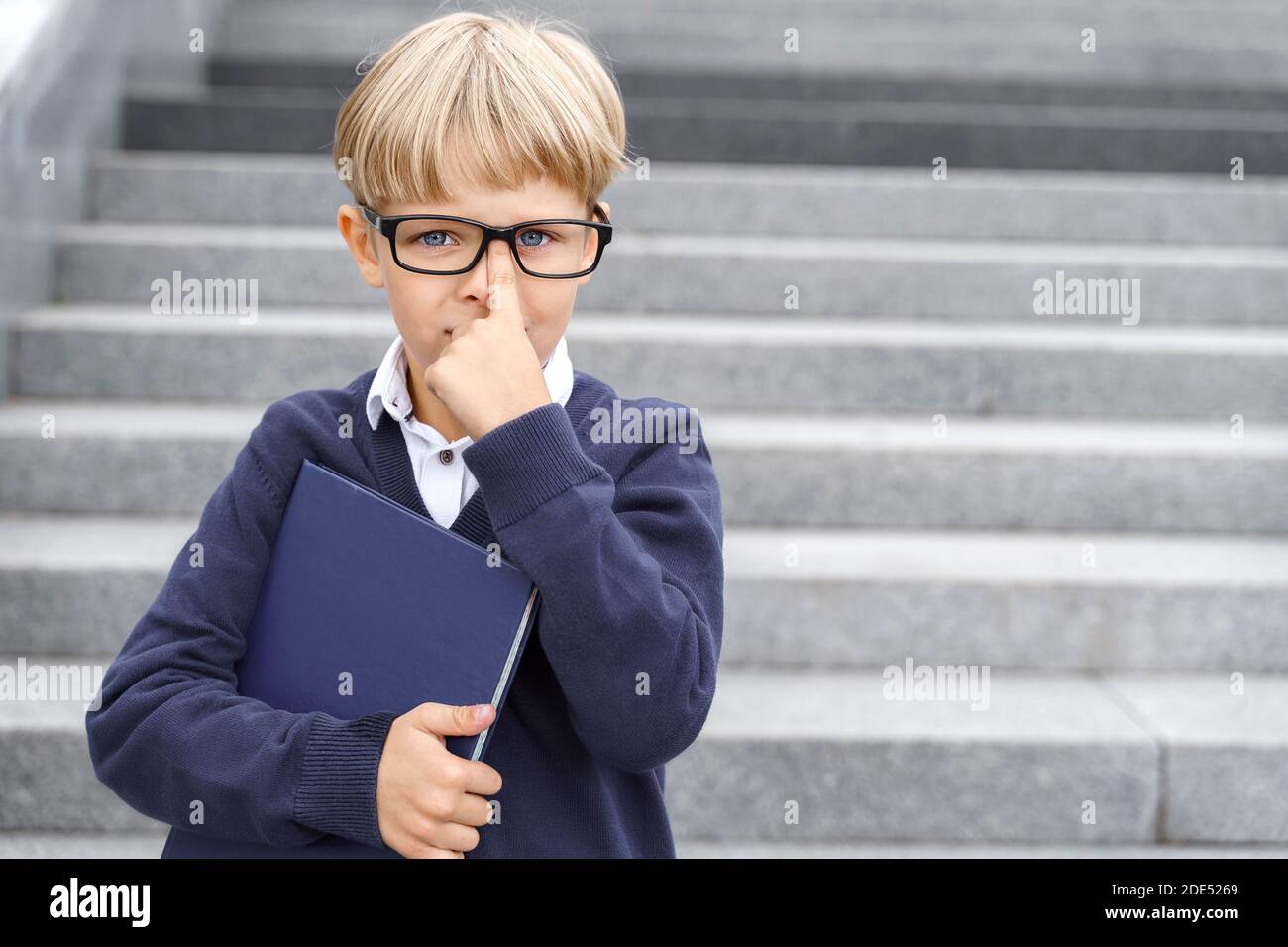 smart boy student in glasses with a blue folder stands on the steps and ...