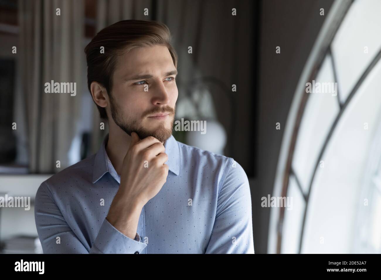 Thoughtful young man leader looking at window visualizing business ...