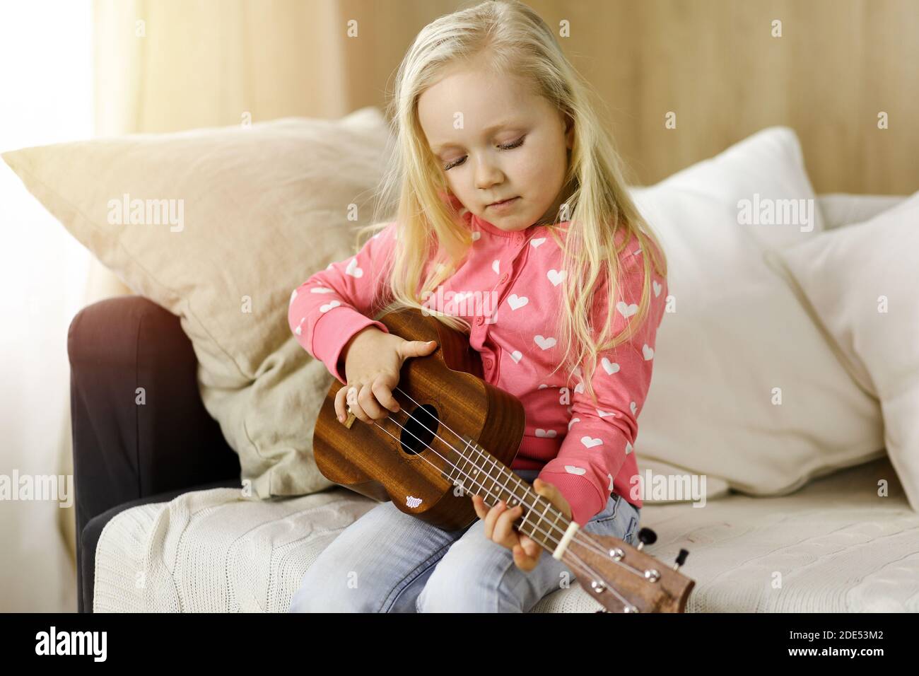 Little cute baby playing ukulele guitarin sunny room. Childhood concept ...