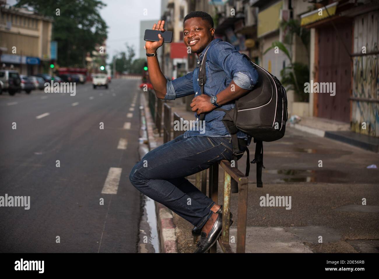 young man sitting on iron bar with backpack greeting smiling Stock ...