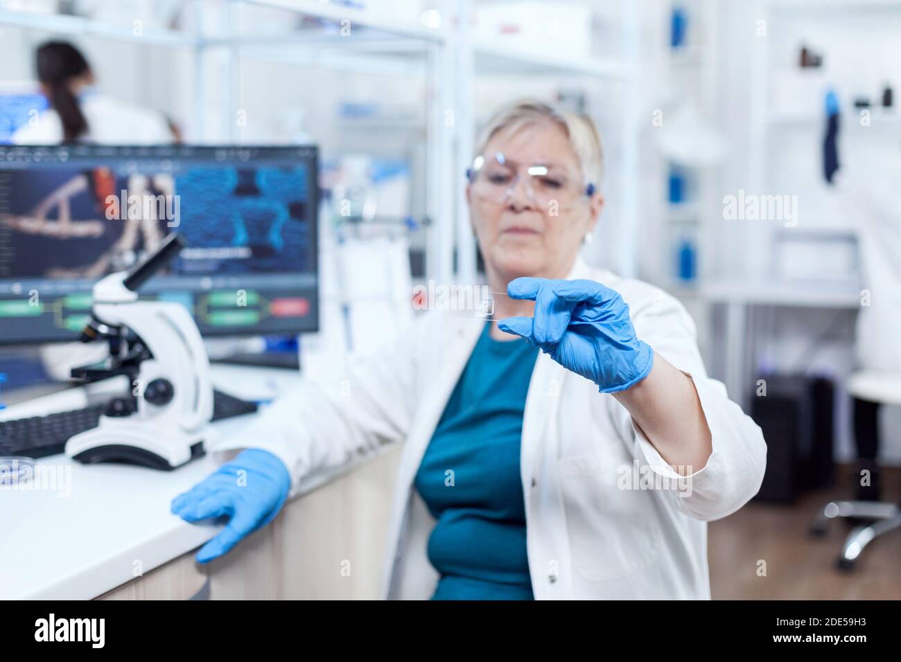 Senior scientist in protective gear holding sample during clinic study ...