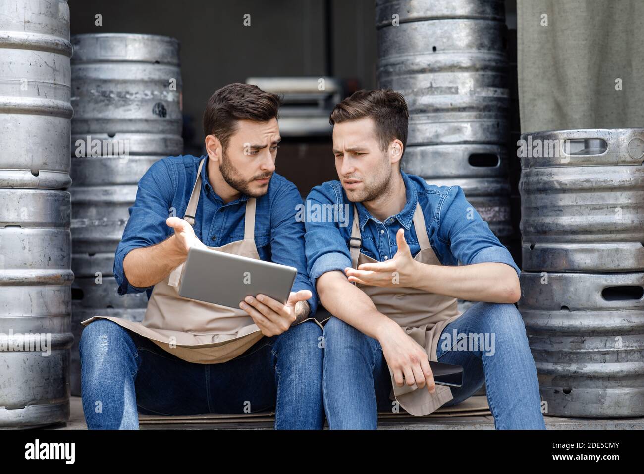 Strong millennial workers in aprons sit, talking, gesticulating and ...