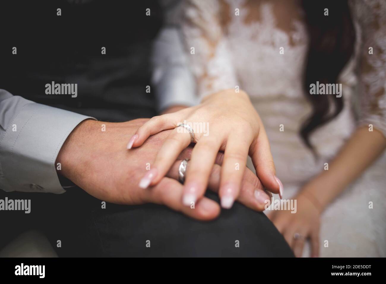 A closeup of a married couple touching hands wearing beautiful wedding ...