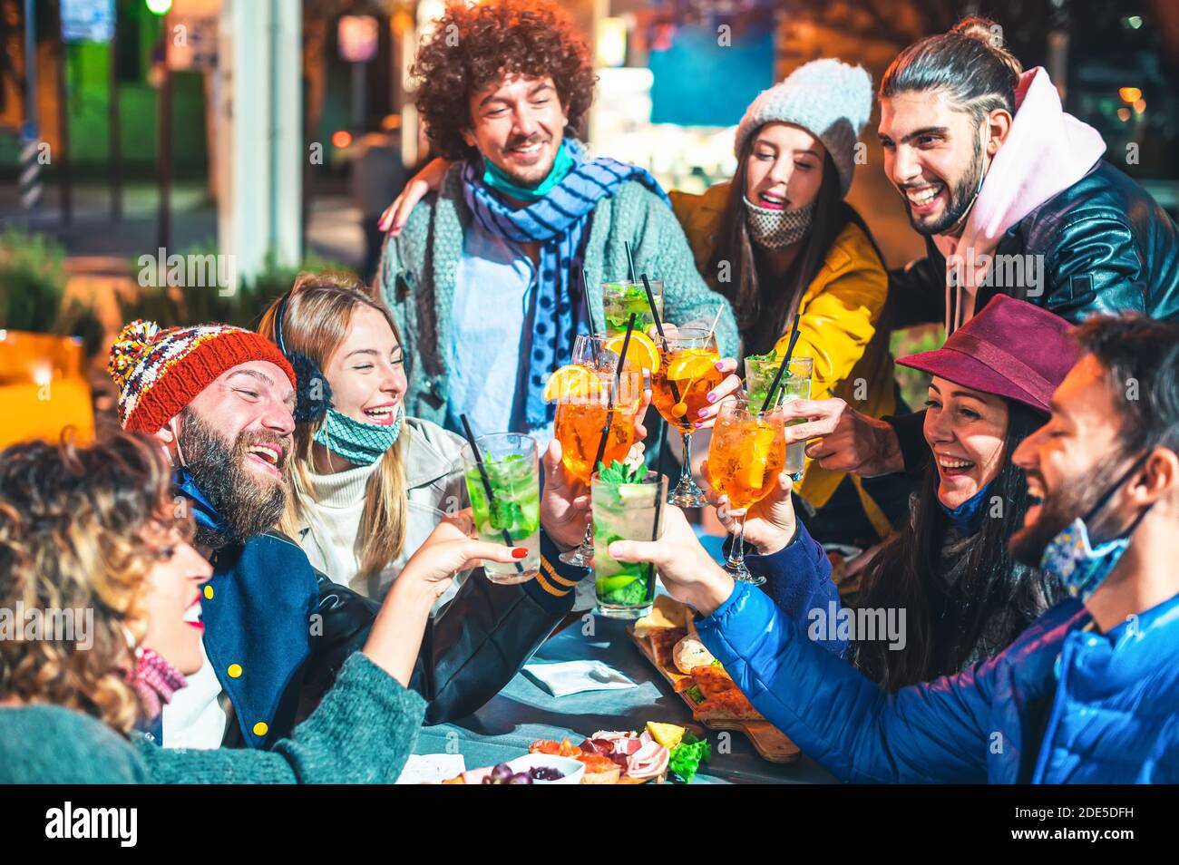 Happy friends toasting fancy drinks at night bar with open mask - New ...