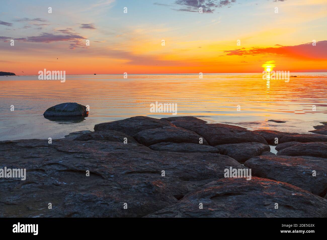 Beautiful colorfull sunset over the sea shore with rocks under shallow ...