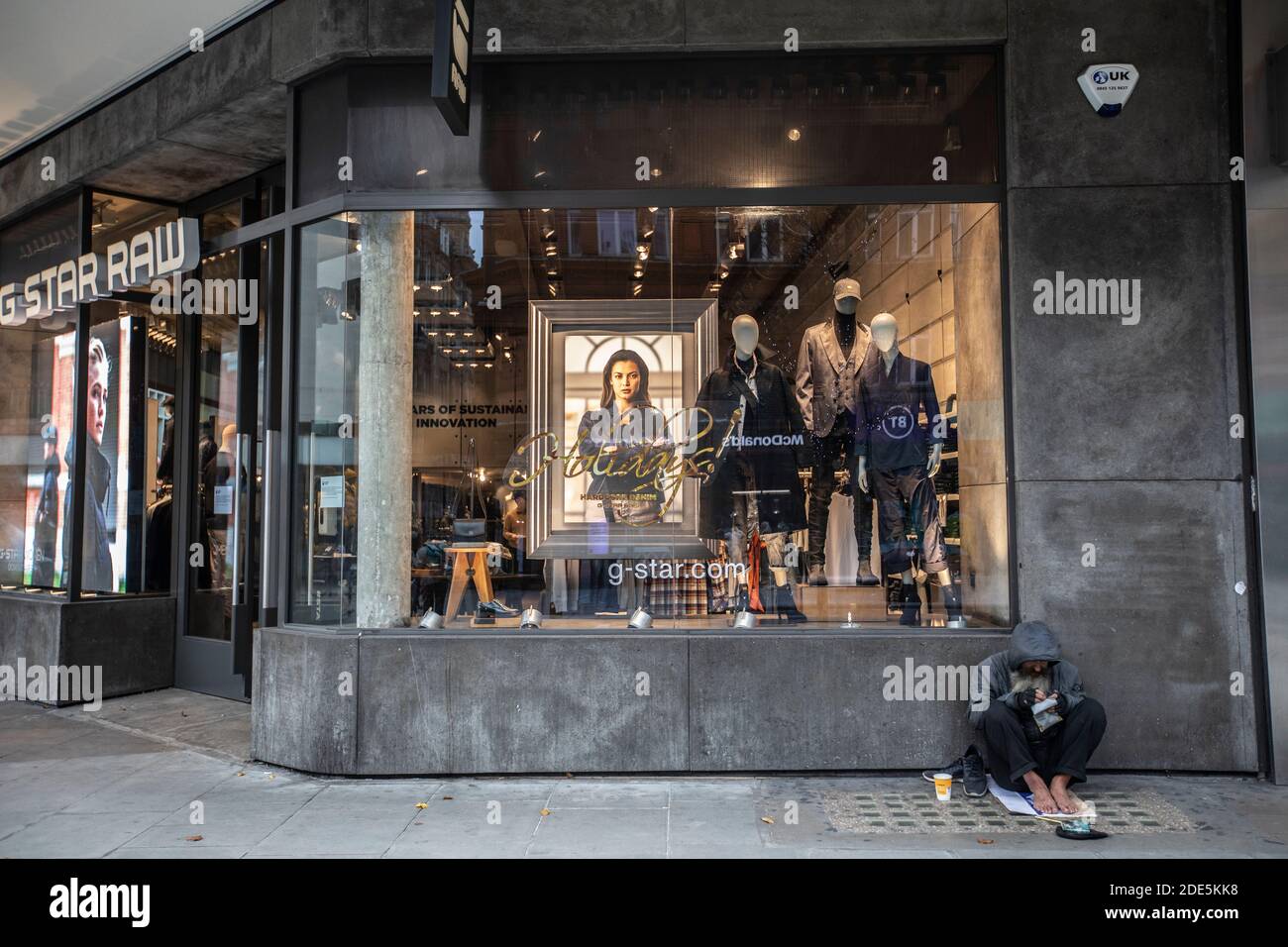 Barefooted homeless man sits alone begging for money outside a clothing ...