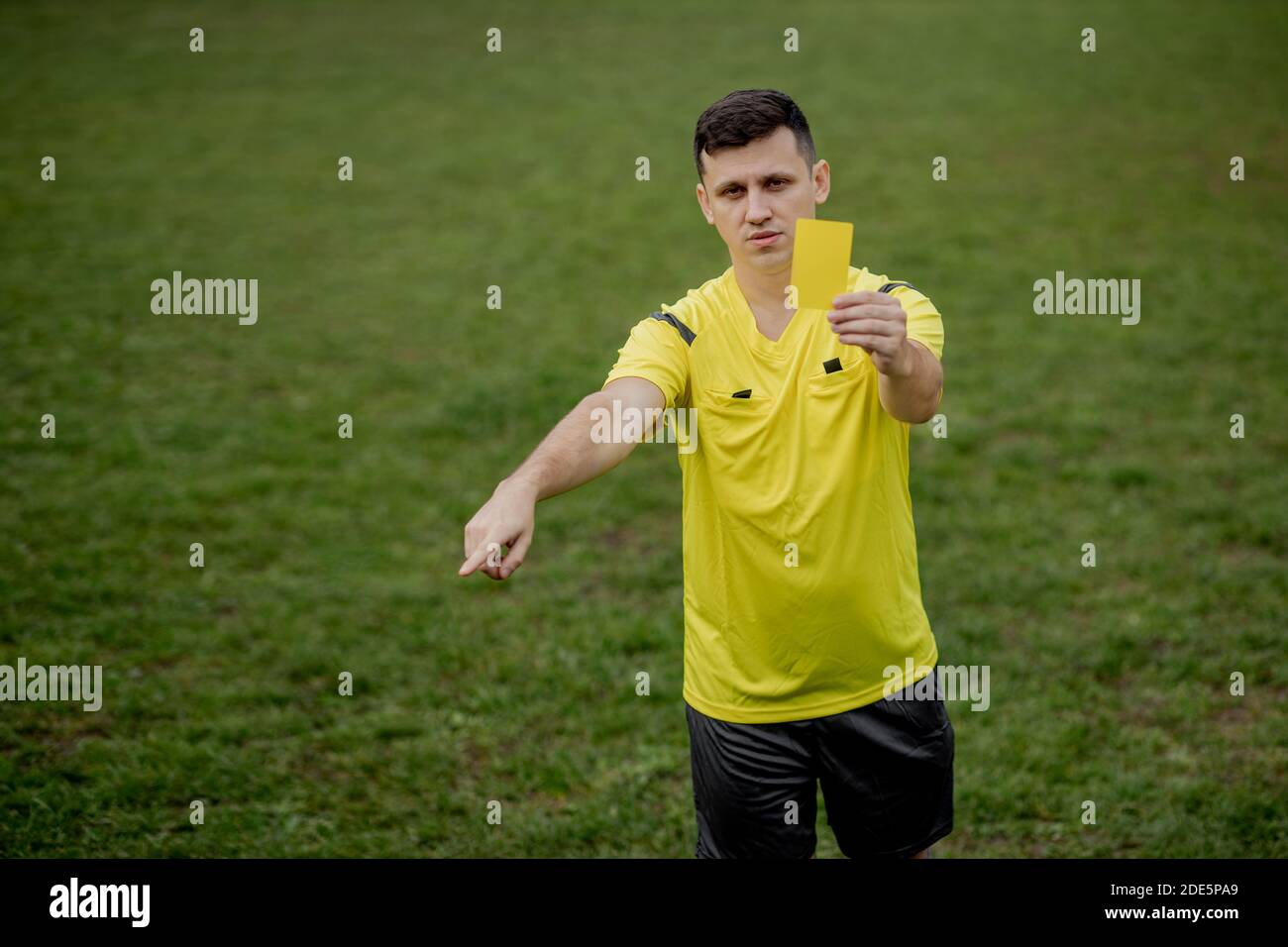Angry football referee showing a yellow card and pointing with his hand ...