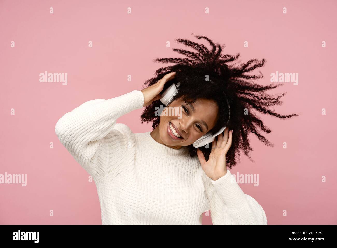 Energized biracial woman sing along, smile broadly, wears wireless ...