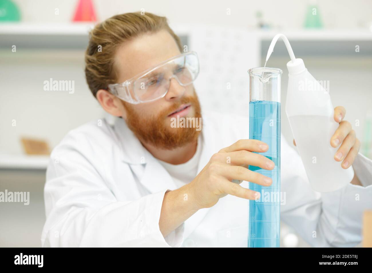 male scientist adding solution to blue liquid in flask Stock Photo - Alamy