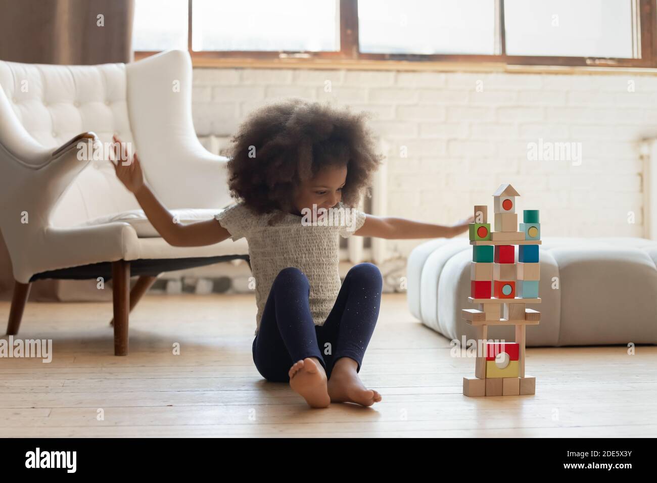 Excited african girl screaming in delight building castle on floor ...