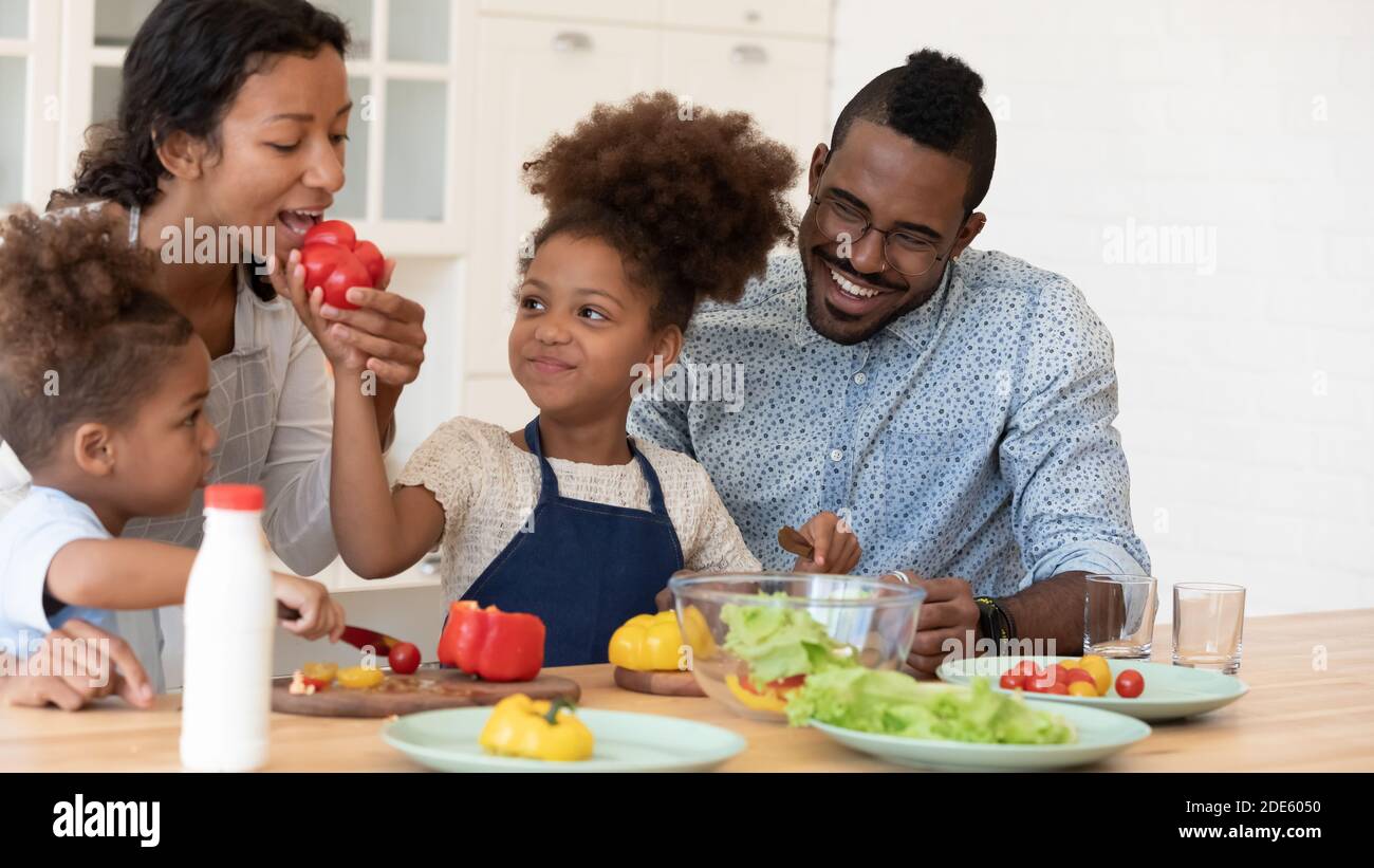 Laughing african couple with two children enjoying cooking at kitchen ...