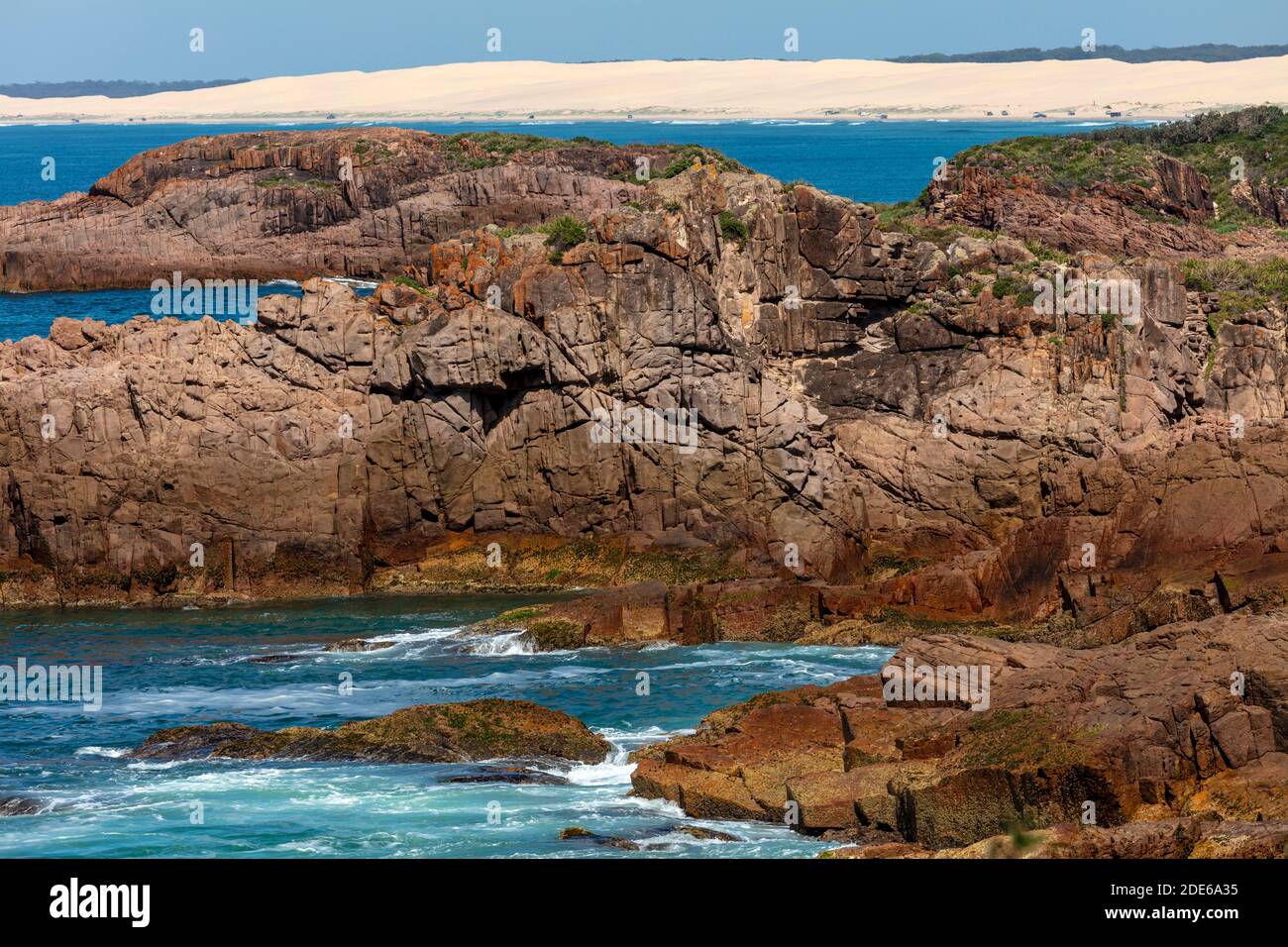The brown Rocks in front of the Stockton Sand Dunes and blue water of ...