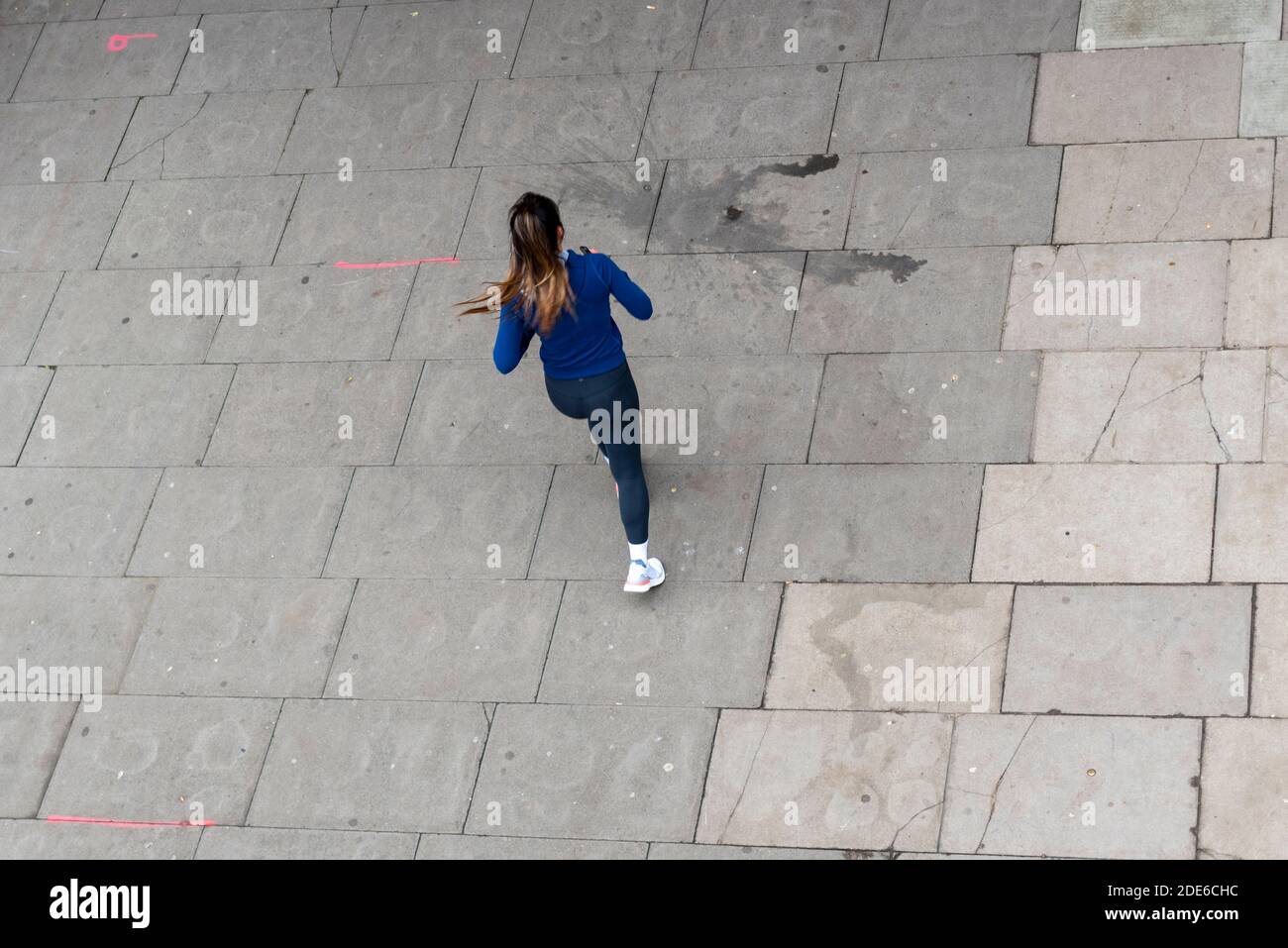 Female jogger, runner, jogging, running, from above. Grey paving slabs ...