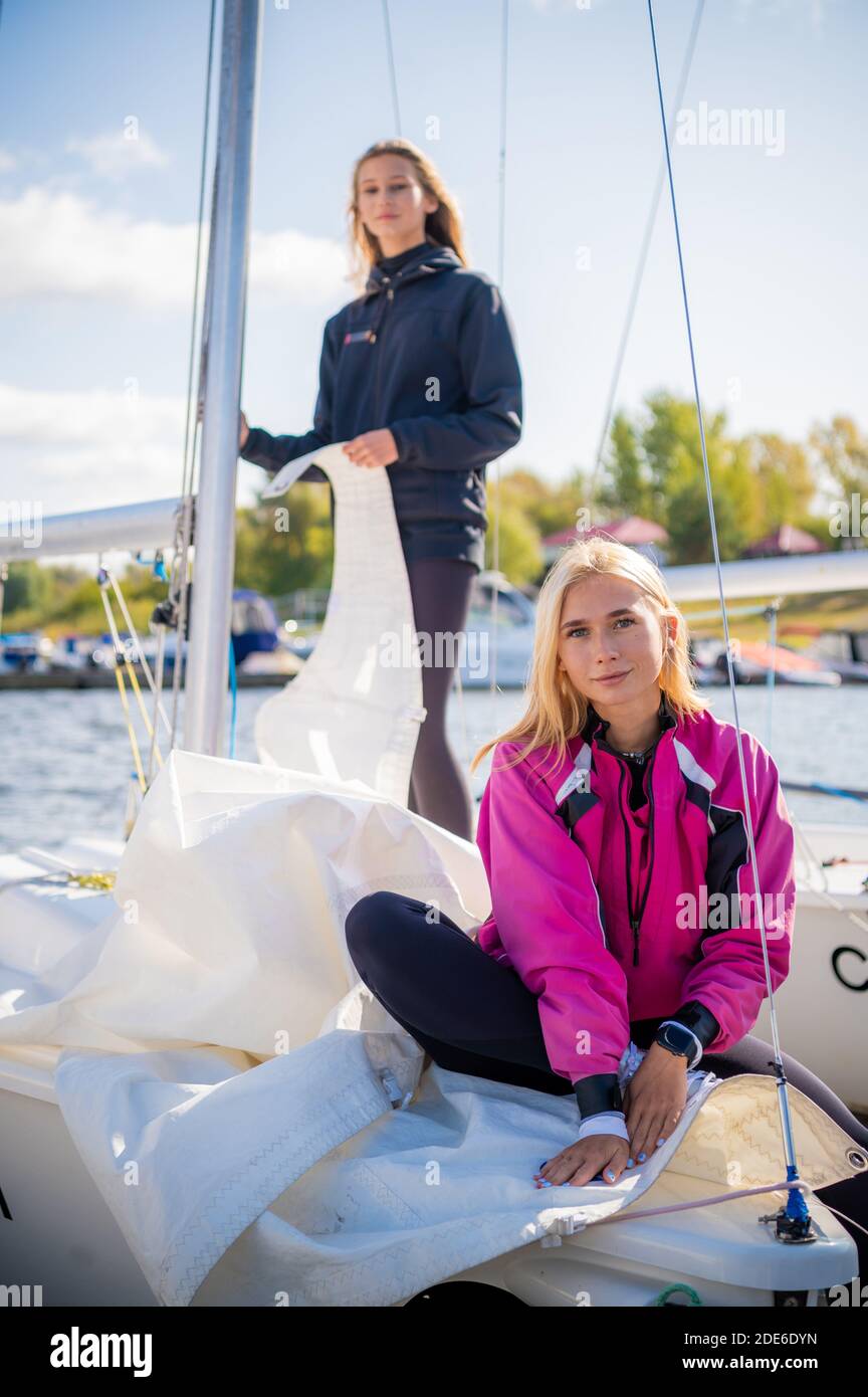 On the pier, two pretty girls pull sails on a boat to participate in a ...