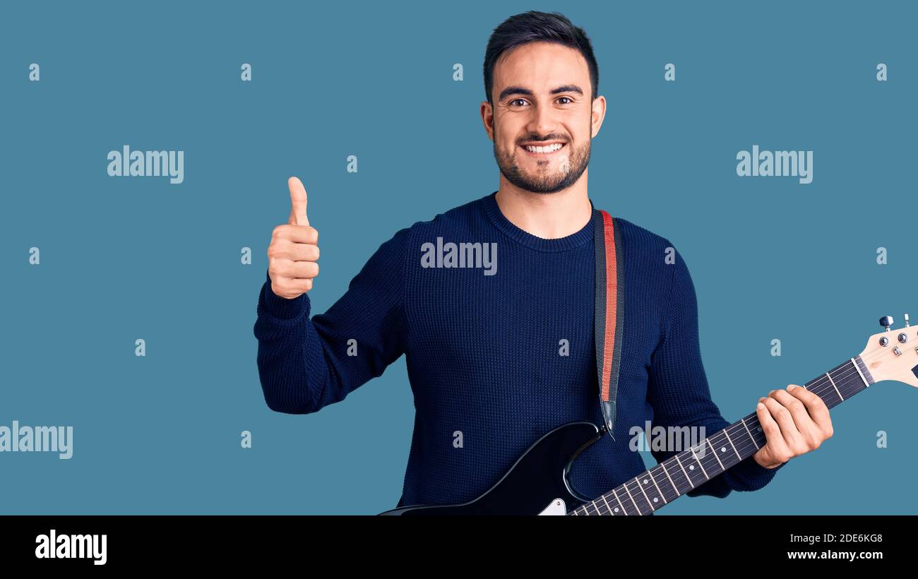 Young handsome man playing electric guitar smiling happy and positive ...