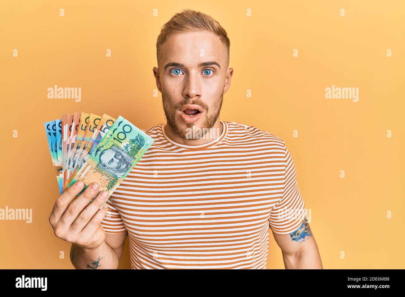 Young caucasian man holding australian dollars scared and amazed with ...