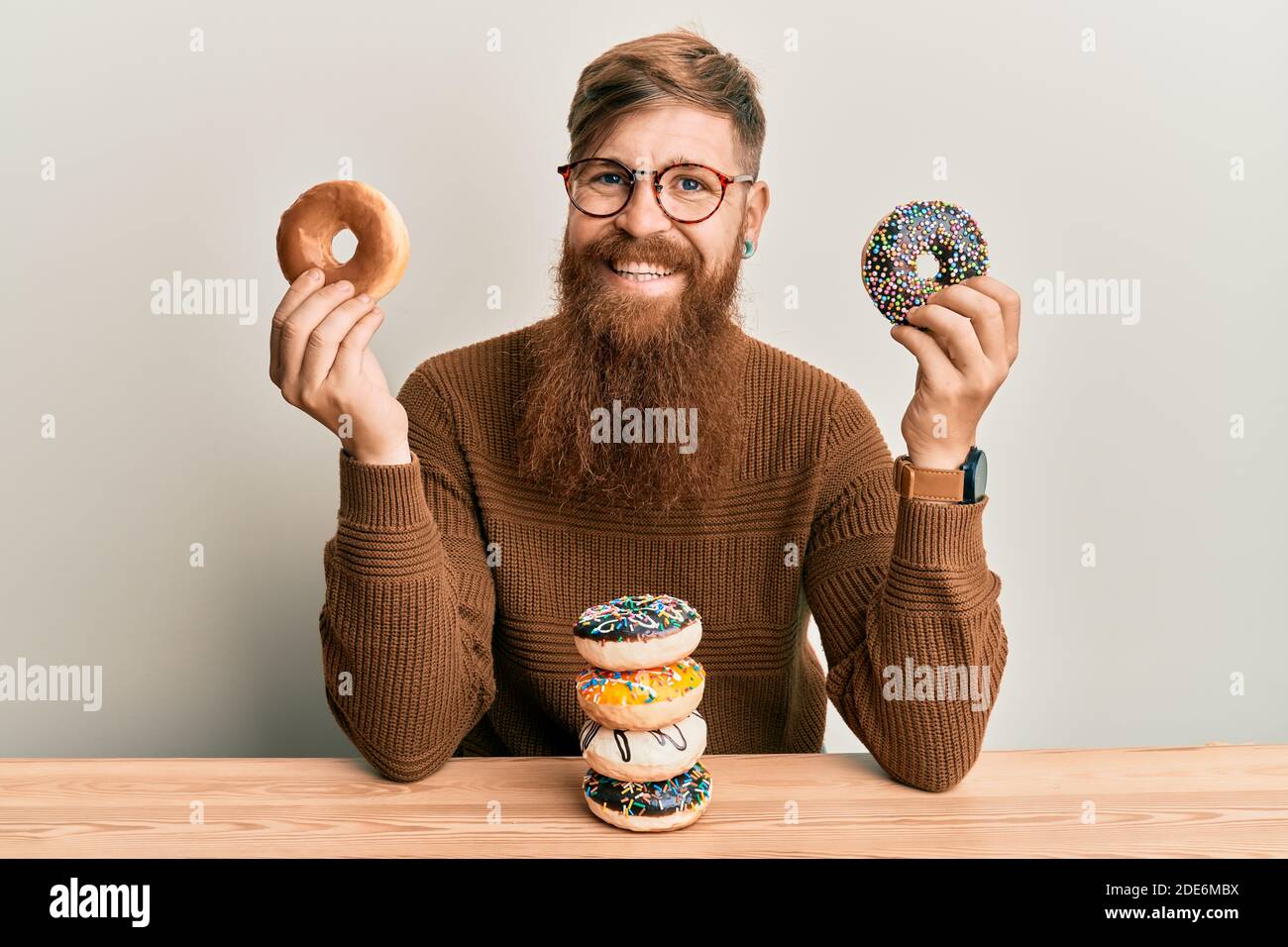 Young irish redhead man eating doughnut for breakfast smiling with a ...