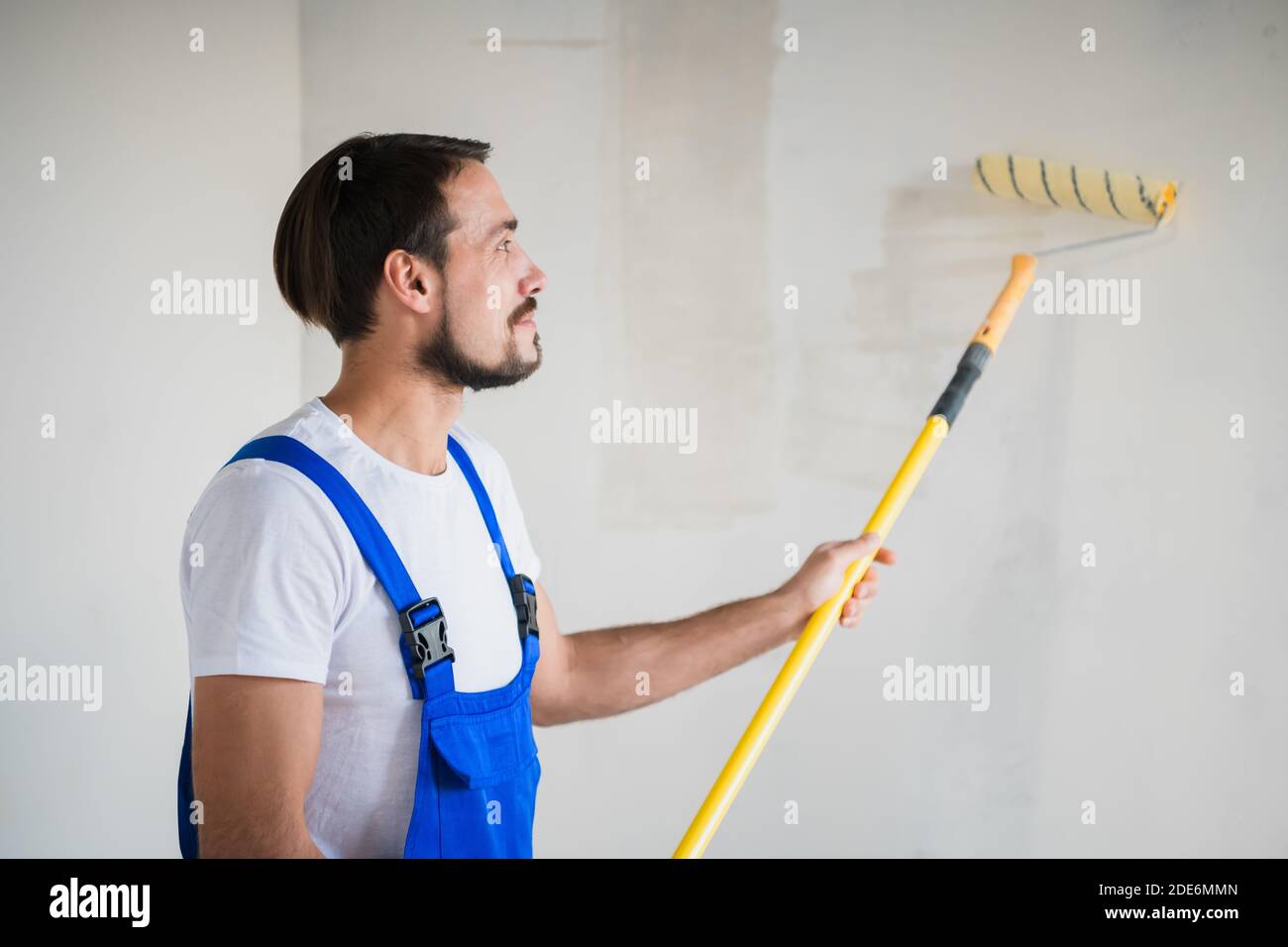 Painter in work clothes paints the wall white with a roller Stock Photo ...