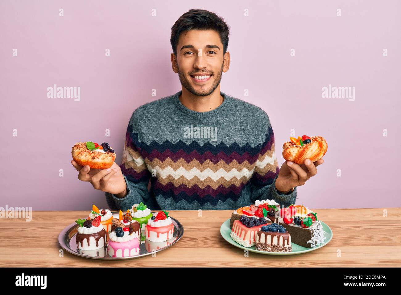 Young handsome man holding sweet pastries smiling with a happy and cool ...