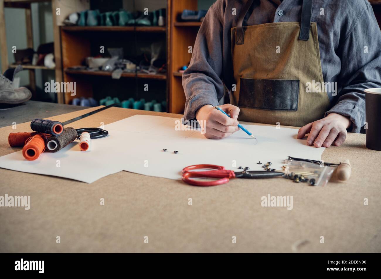 A young shoemaker makes a drawing for a pattern for leather shoes on a ...