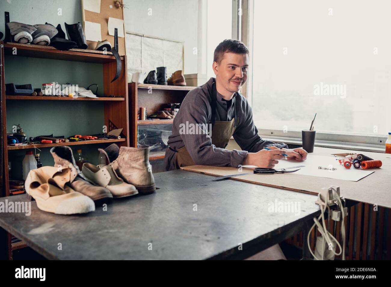 A young shoemaker makes a drawing for a pattern for leather shoes on a ...