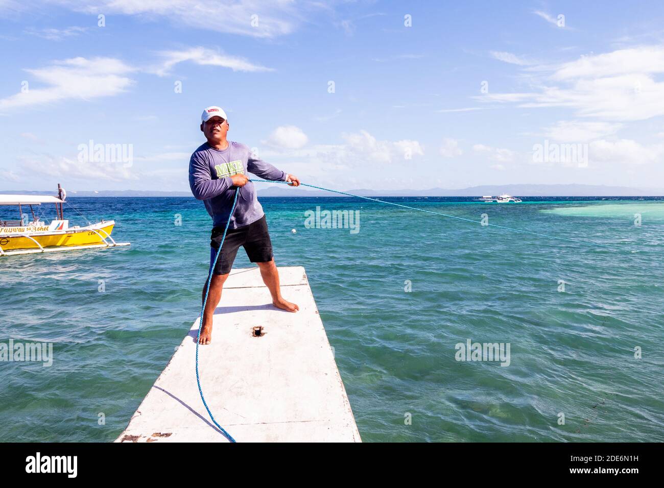 A Filipino seafarer pulling on a rope to dock his outrigger boat off ...