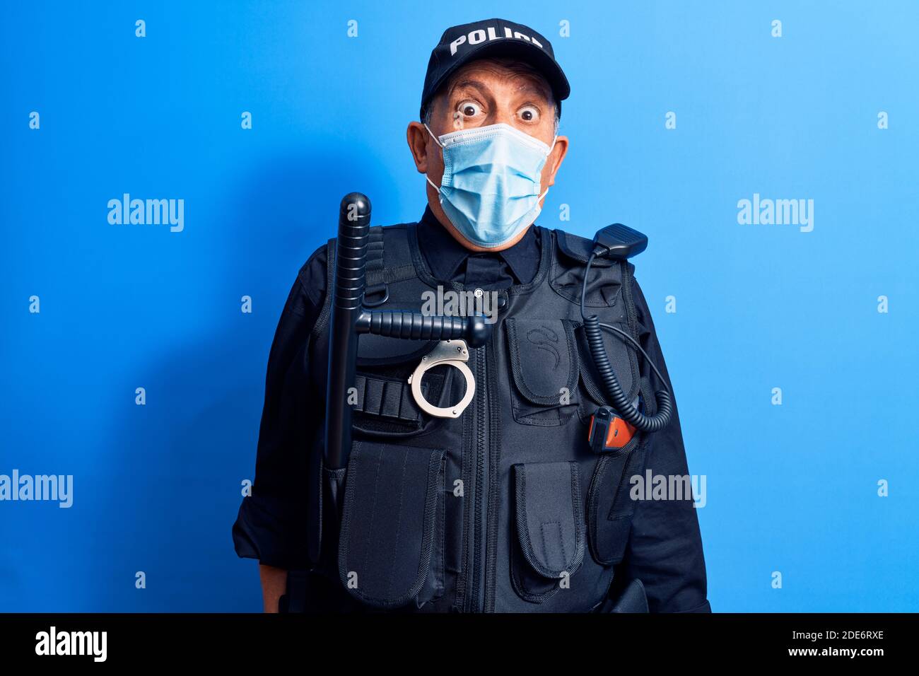 Senior police man wearing surgical mask scared and amazed with open ...