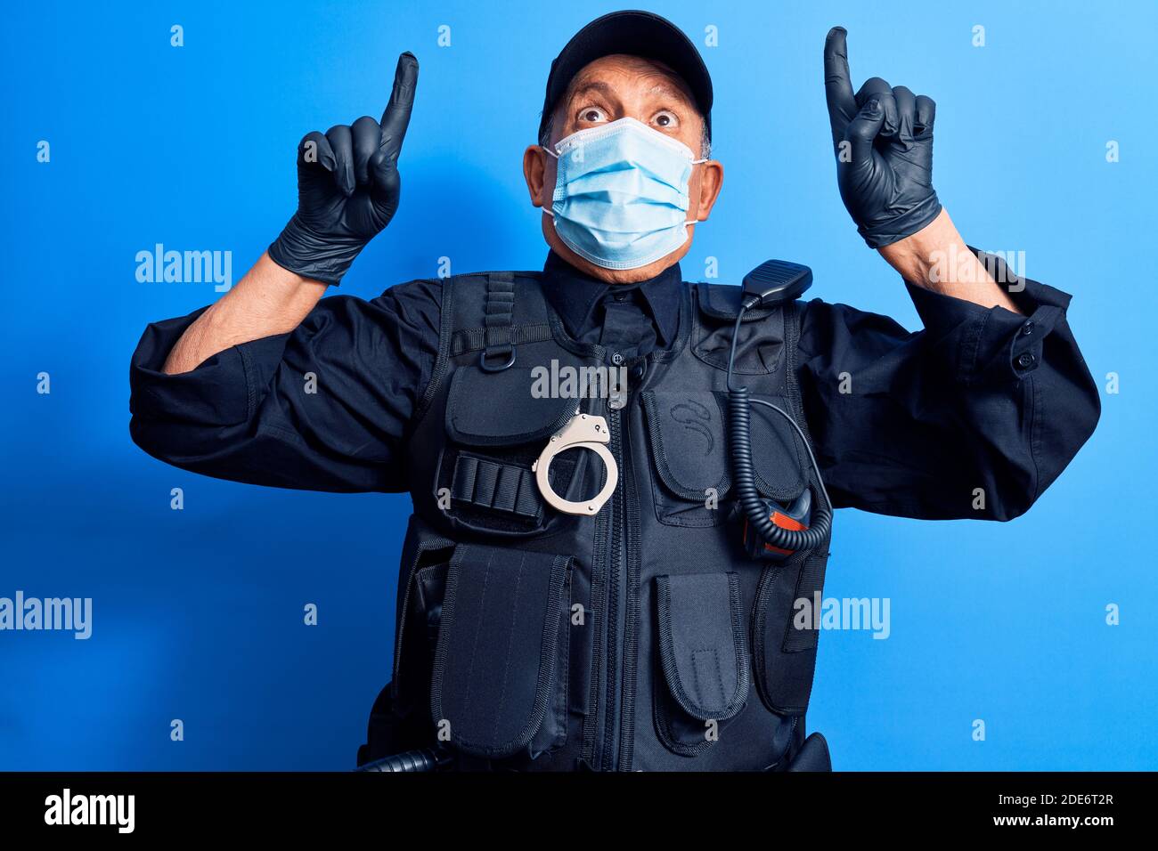Senior police man wearing surgical mask amazed and surprised looking up ...