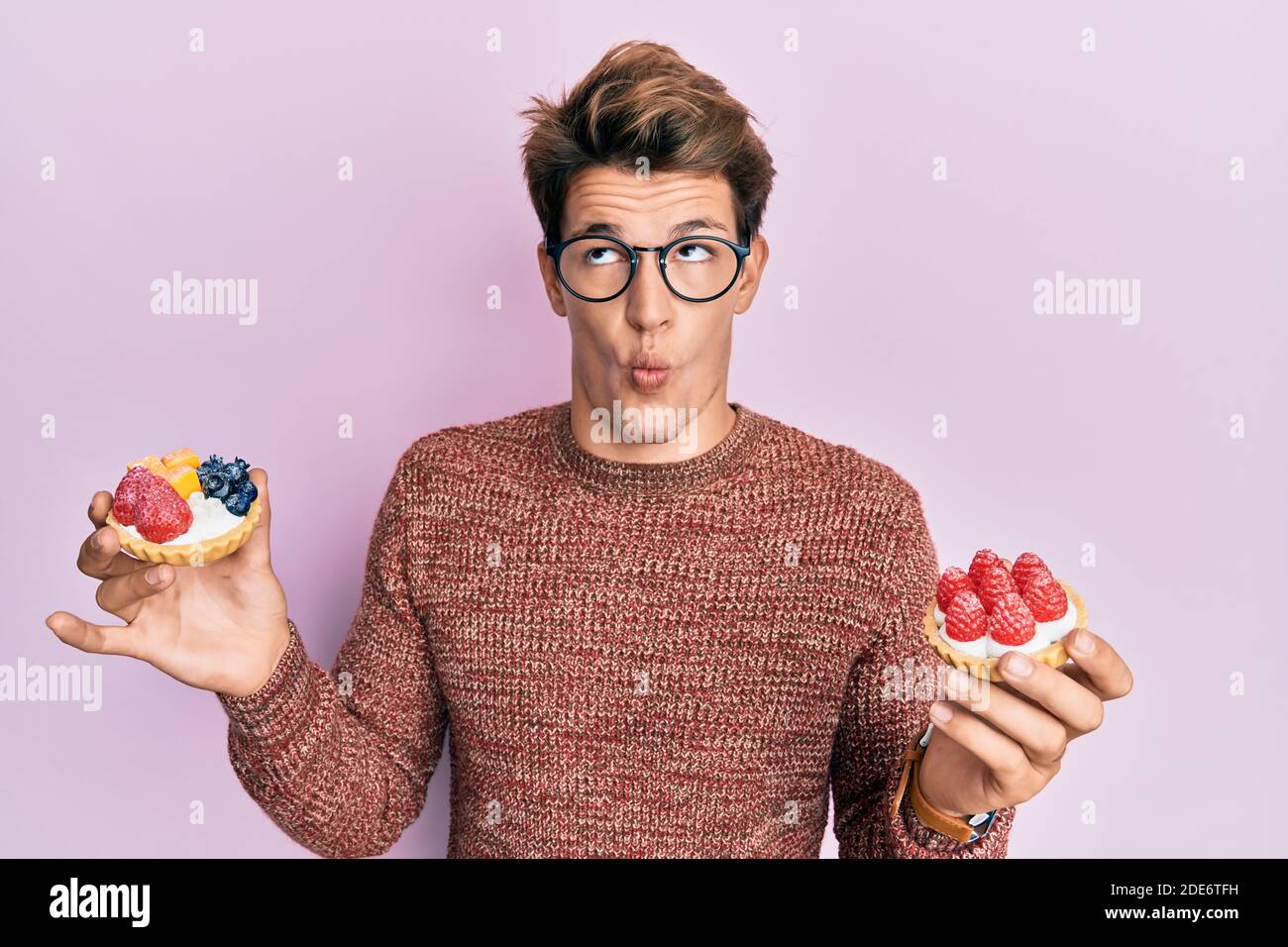 Handsome caucasian man holding cake slices making fish face with mouth ...