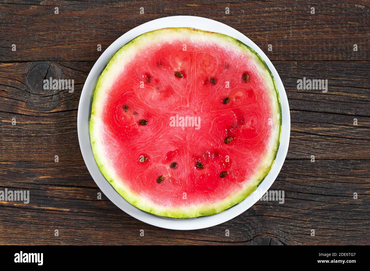 Round watermelon slice in plate on dark wooden background. View from ...