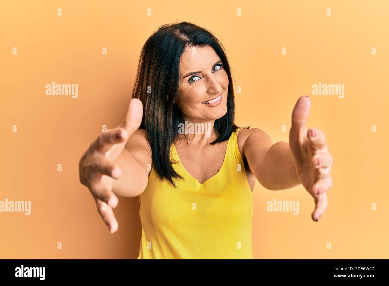 Middle age brunette woman wearing casual clothes over yellow background ...