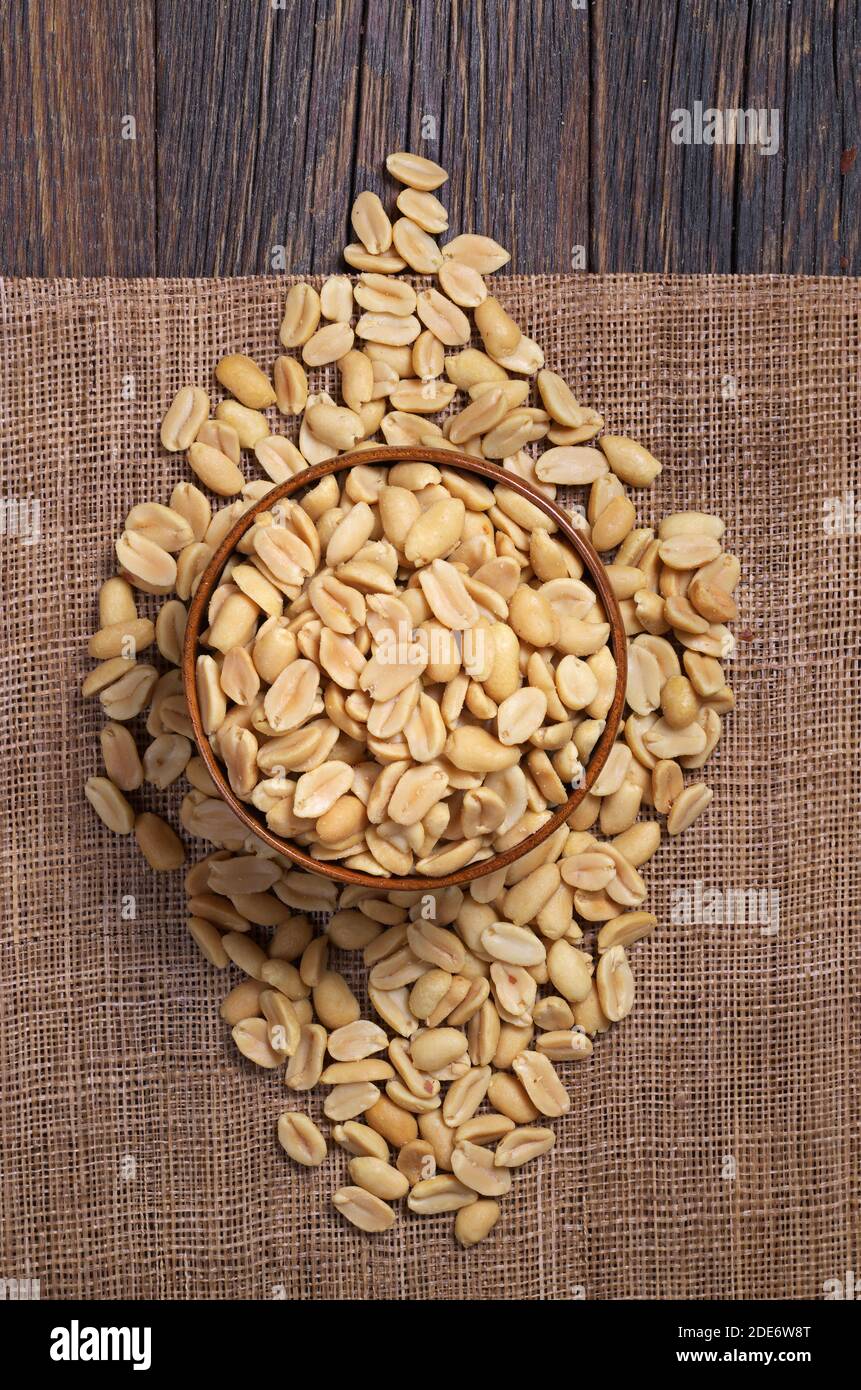Halves of roasted peanuts in bowl and near on dark wooden background ...