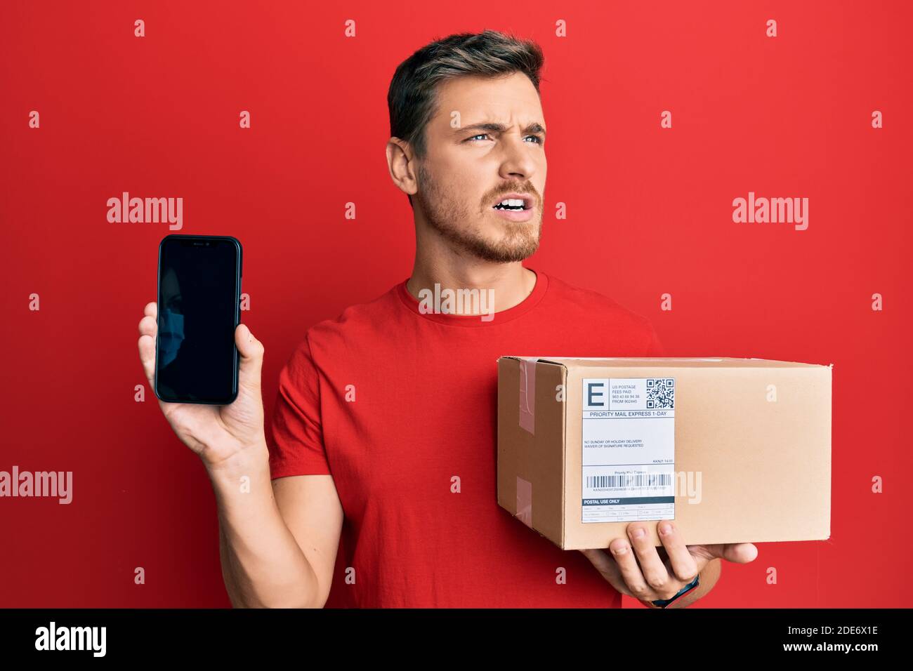 Handsome caucasian man holding delivery package and showing smartphone ...