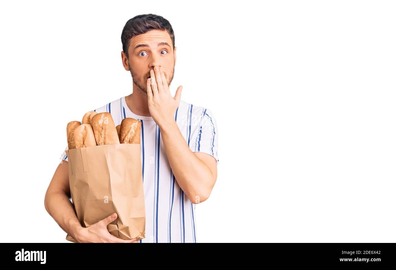Handsome young man with bear holding paper bag with bread covering ...