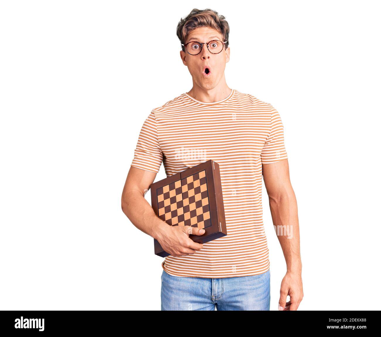 Young handsome man holding chess scared and amazed with open mouth for ...