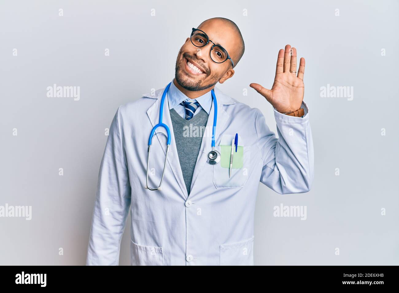 Hispanic adult man wearing doctor uniform and stethoscope waiving ...