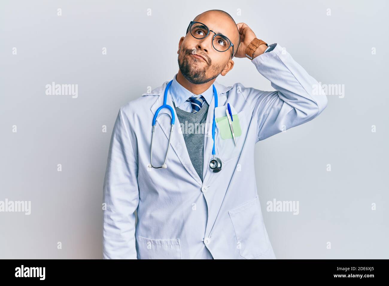Hispanic adult man wearing doctor uniform and stethoscope confuse and ...