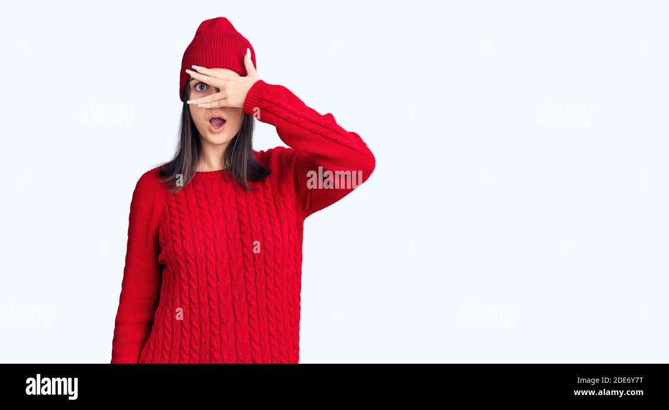 Young beautiful girl wearing sweater and wool cap peeking in shock ...