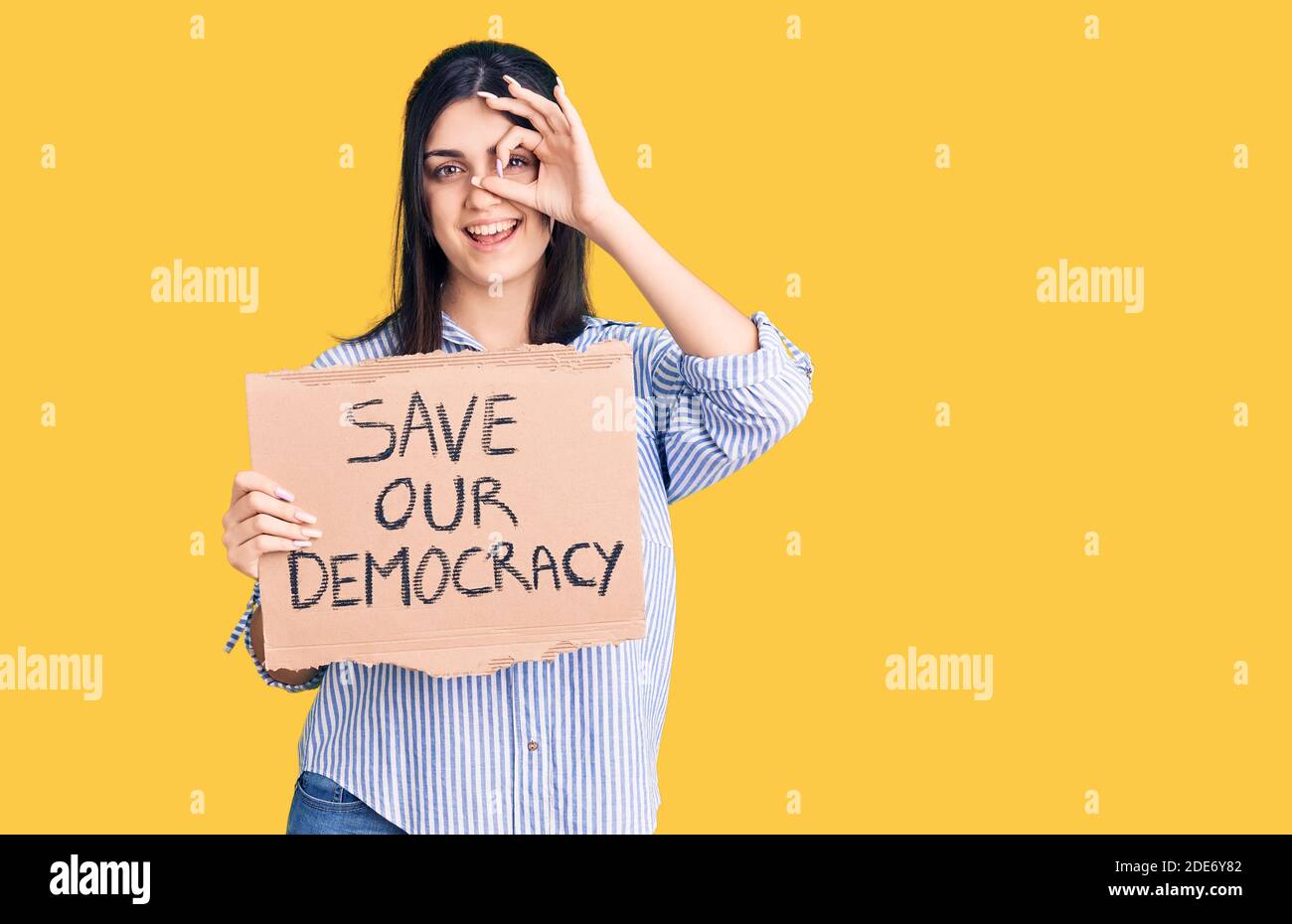 Young beautiful girl holding save our democracy cardboard banner ...