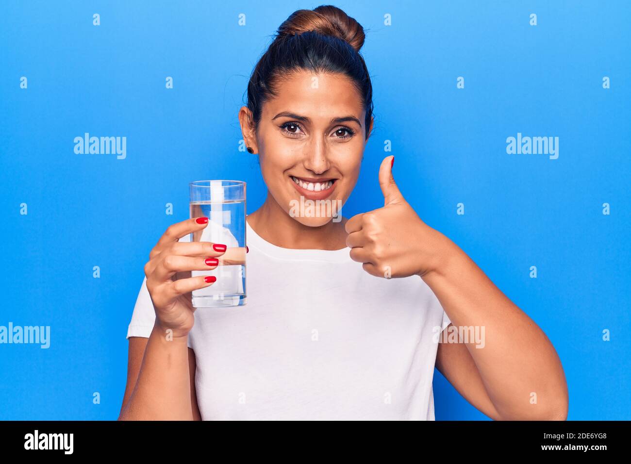 Young beautiful brunette woman drinking glass of water smiling happy ...