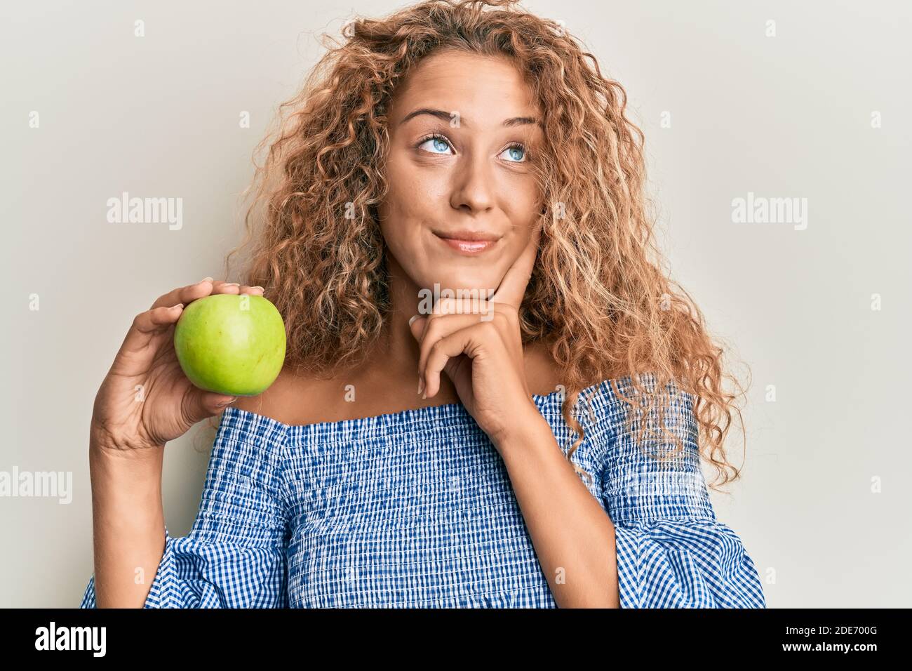 Beautiful caucasian teenager girl holding green apple serious face ...
