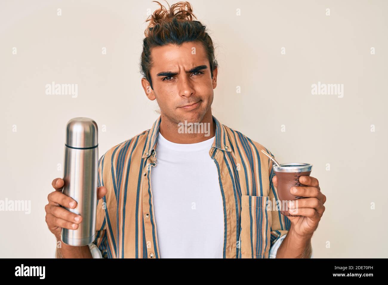 Young hispanic man drinking mate infusion clueless and confused ...