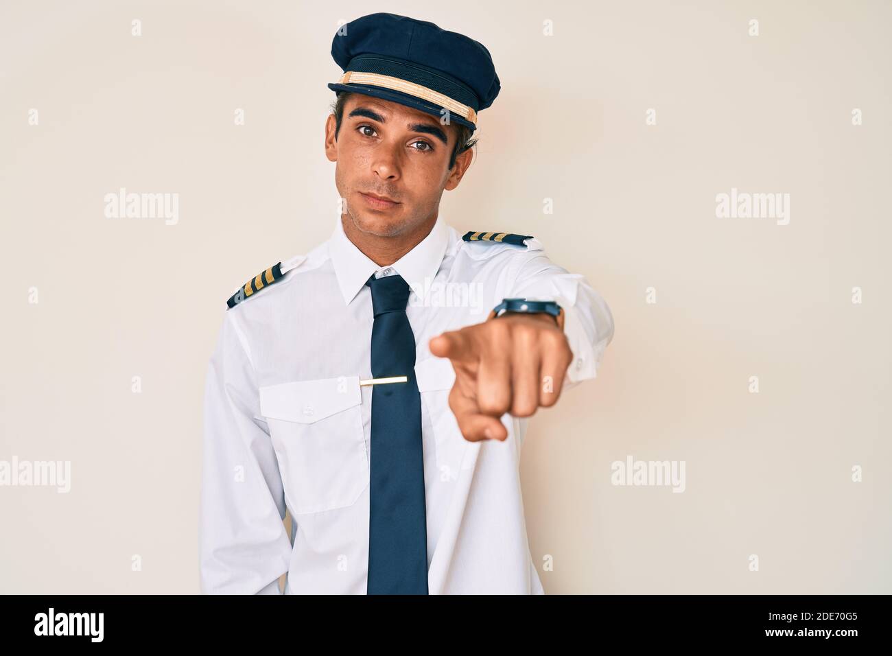 Young hispanic man wearing airplane pilot uniform pointing displeased ...