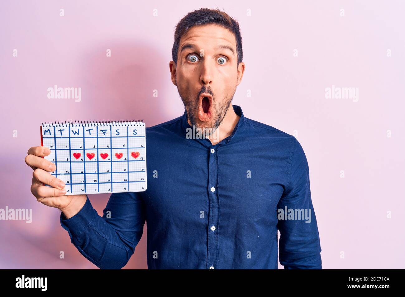 Young handsome man holding calendar with red hearts on week over pink ...