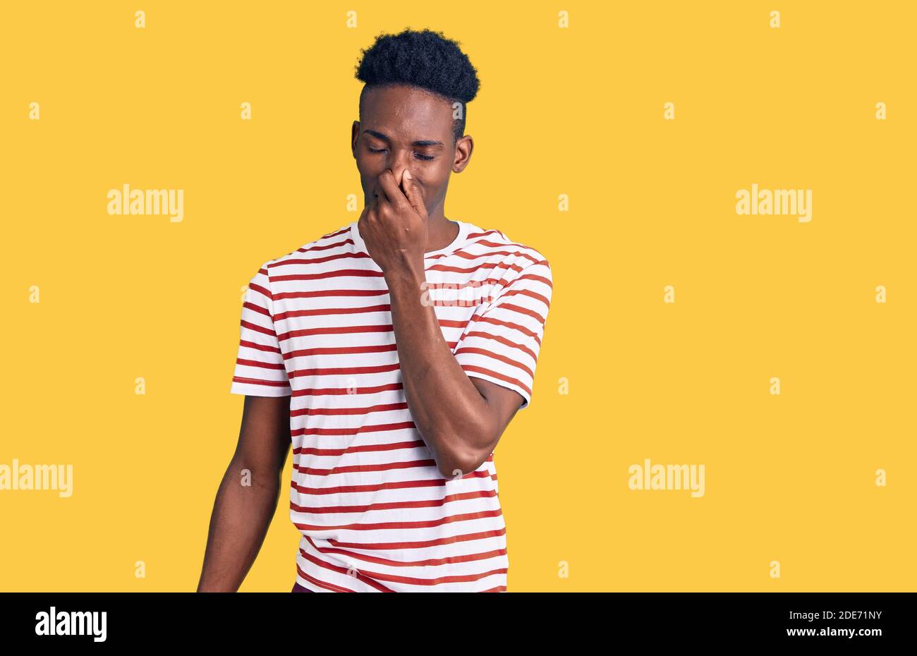 Young african american man wearing casual clothes smelling something ...