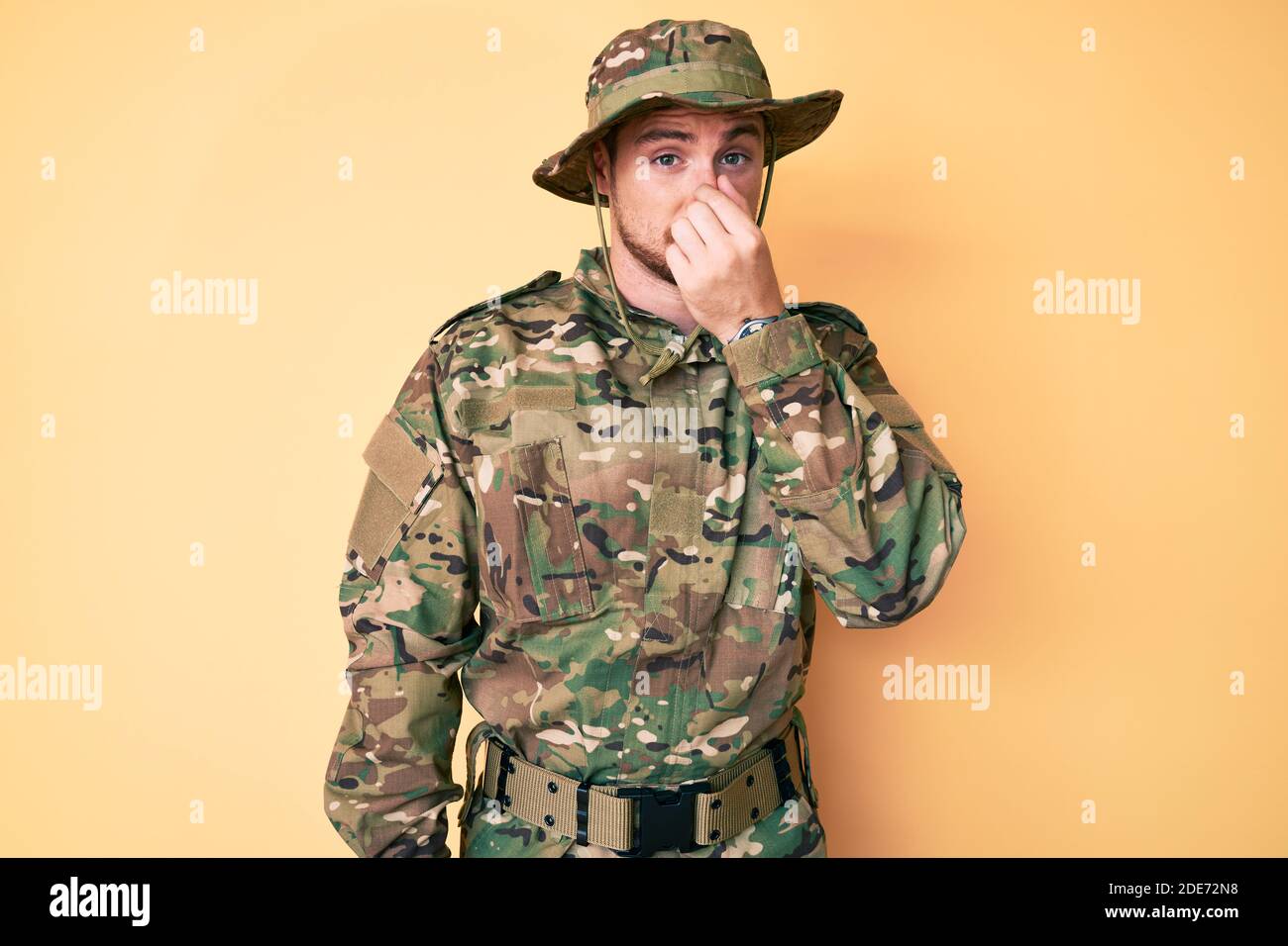 Young caucasian man wearing camouflage army uniform smelling something ...